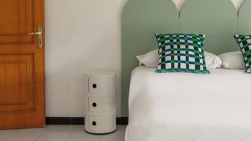 Quarto com porta de madeira, mesa de cabeceira branca com gavetas e cama com almofadas de padrão xadrez verde e branco.