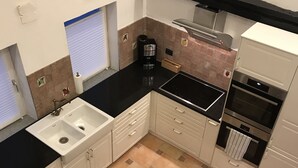 Cozinha compacta com bancada preta, armários brancos, forno embutido e mesa de jantar de madeira com cadeiras.