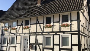 Uma casa tradicional de enxaimel com várias janelas, algumas com caixas de flores, e um telhado em tijolos.
