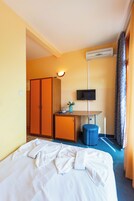 Quarto de hotel com cama, escrivaninha, televisão de tela plana, guarda-roupa e ar condicionado.