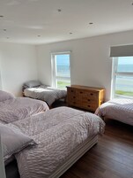 Quarto com duas camas, cômoda de madeira e grandes janelas com vista para o mar.