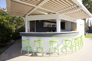 Uma área de bar com balcão, banquetas e um espaço de estar coberto.