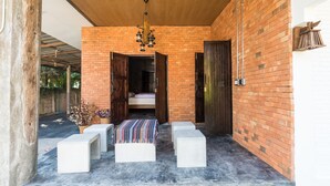 Quarto com parede de tijolos, cama com manta listrada e luminária pendente.