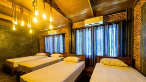 Quarto de hotel com quatro camas de solteiro, cabeceiras de madeira e parede de tijolos.