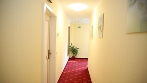 Um corredor com carpete vermelho, uma porta, um vaso de planta e um quadro na parede.