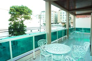 Varanda com cadeiras e mesa brancas, com vista para um horizonte urbano repleto de edifícios.