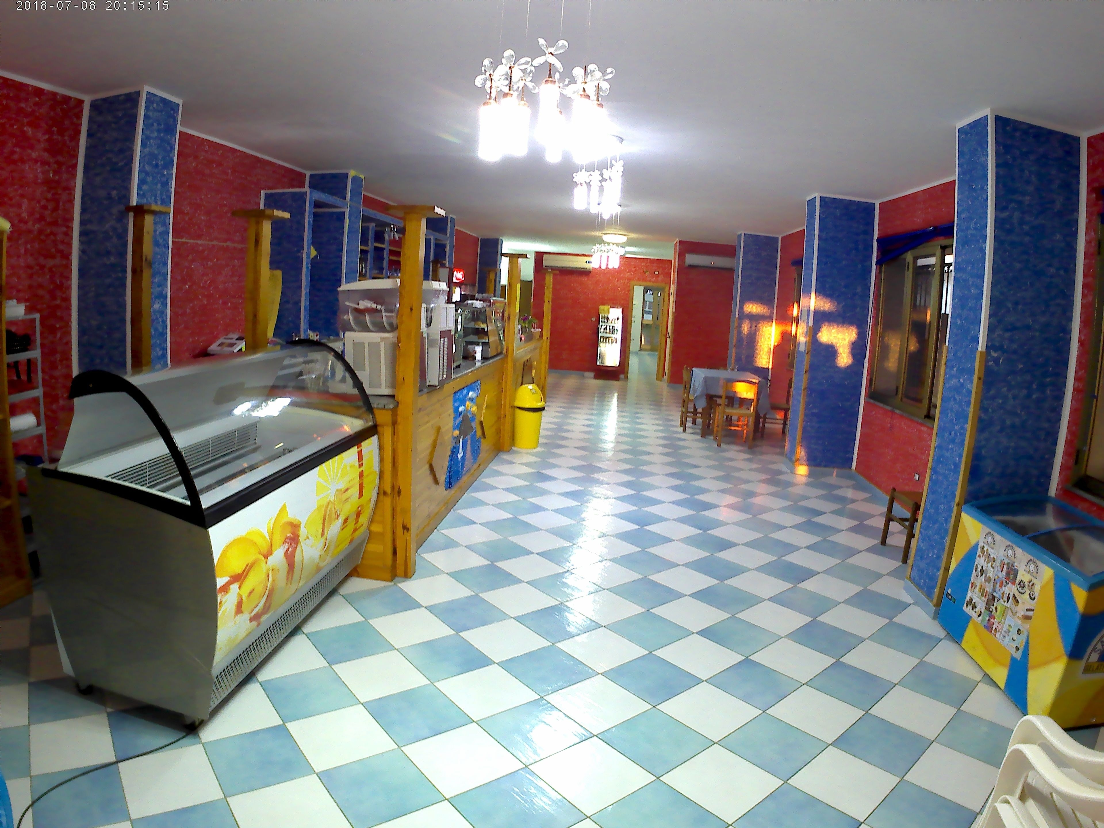 Um quarto colorido com um chão xadrez, um balcão de exposição de comida e uma mesa com cadeiras.