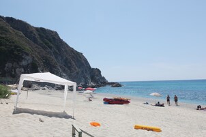 Uma praia com uma tenda branca, caiaques e um penhasco rochoso.