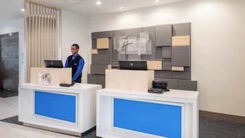 Uma área de recepção de hotel com dois balcões e um design moderno na parede, com uma pessoa de pé atrás de um dos balcões.