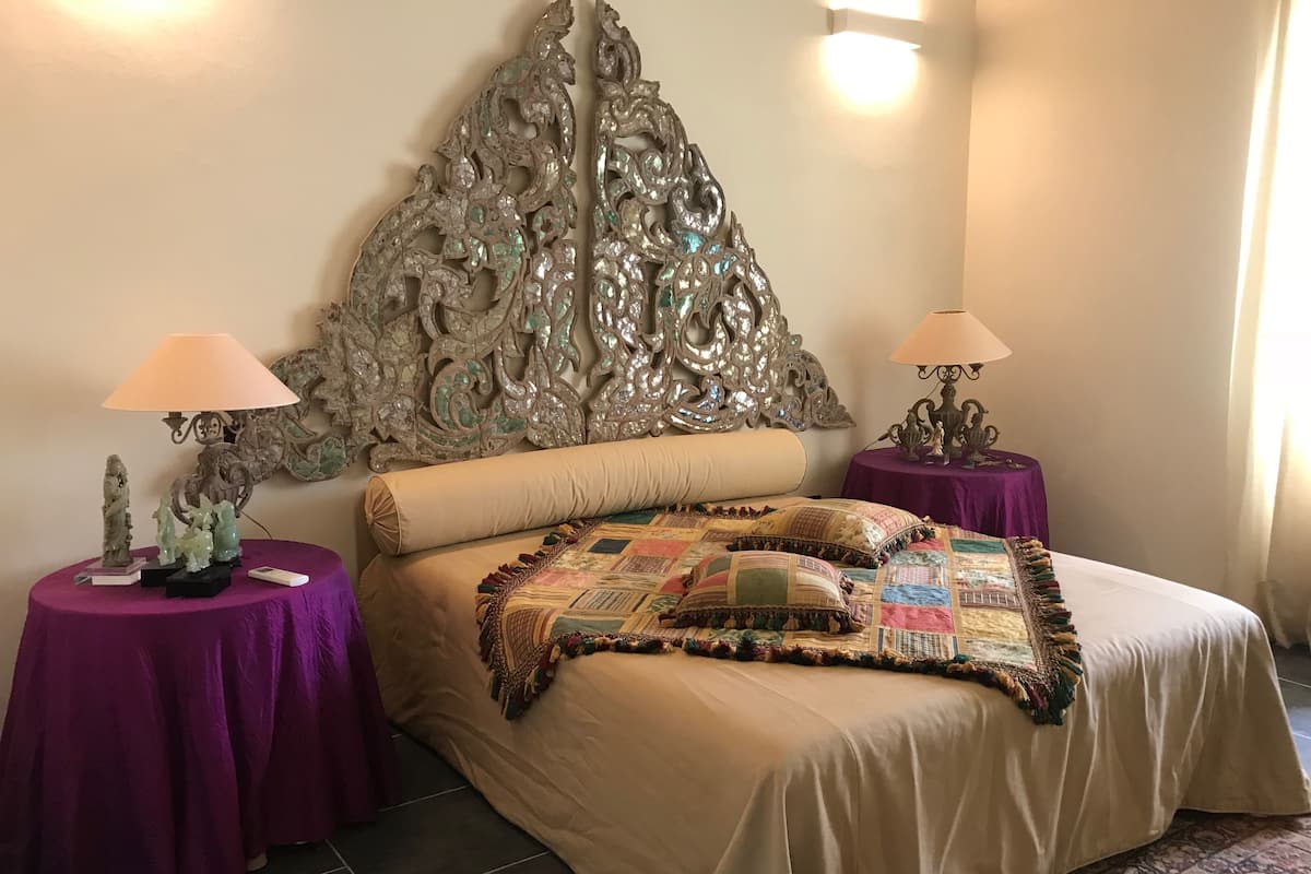 Quarto bem arrumado com uma cama grande, duas mesas laterais com abajures e um objeto decorativo na parede.