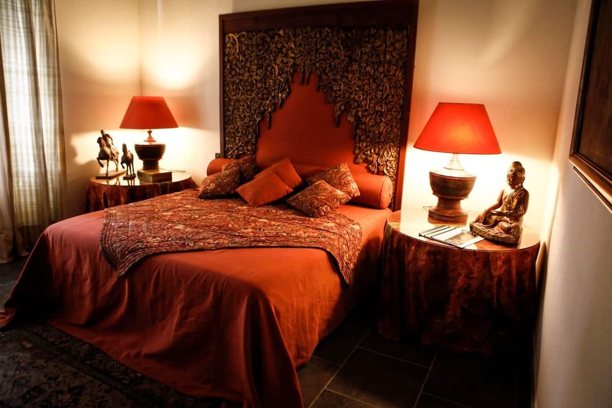 Quarto bem iluminado com uma cama grande, duas mesas de cabeceira com abajures e objetos decorativos.