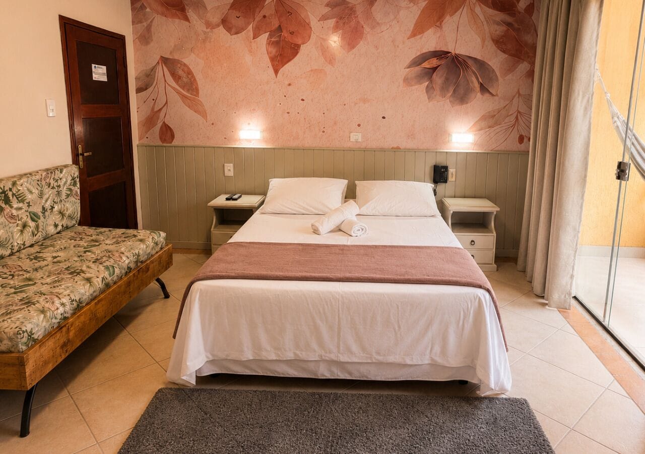 Quarto de hotel com cama, sofá, mesa de cabeceira e parede com padrão de folhas.