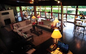 Uma sala de estar espaçosa com lareira, assentos confortáveis e grandes janelas com vista para o verde.