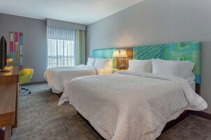 Quarto de hotel com duas camas, uma escrivaninha, uma cadeira e uma televisão.