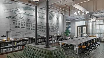 Uma biblioteca moderna com um grande mural, assentos de couro verde e uma longa mesa com cadeiras.