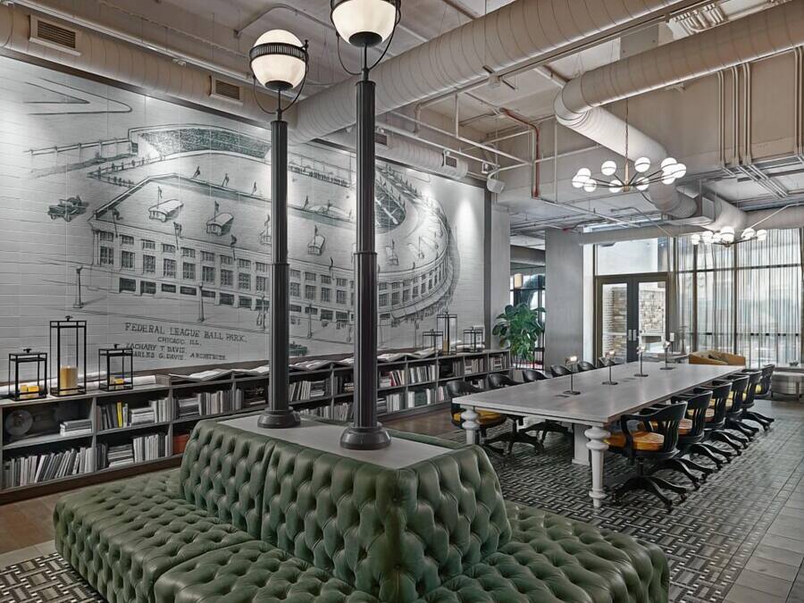 Uma biblioteca moderna com um grande mural, assentos de couro verde e uma longa mesa com cadeiras.