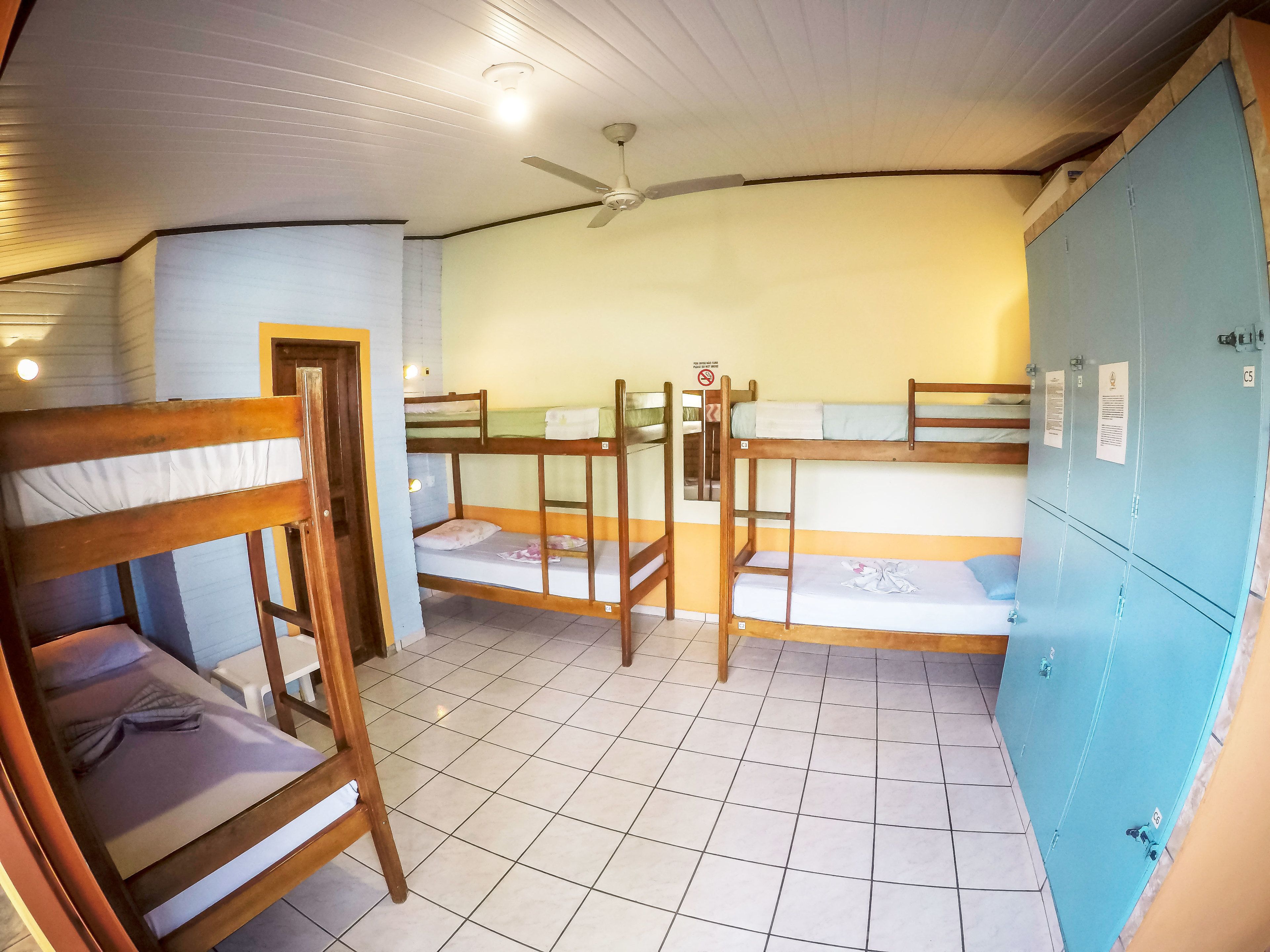 Quarto em dormitório com beliches, ventilador de teto e guarda-roupa azul.