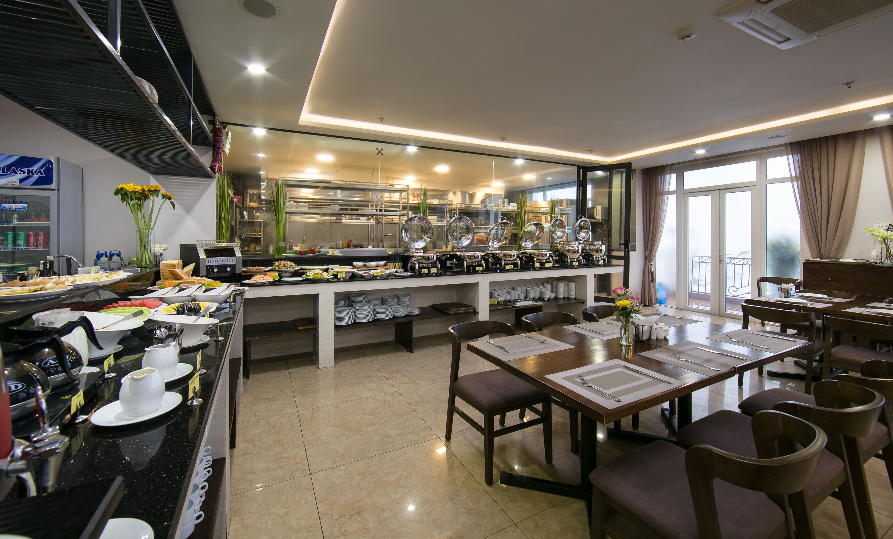 Disposição de buffet com diversos alimentos e uma área de estar com mesas e cadeiras.