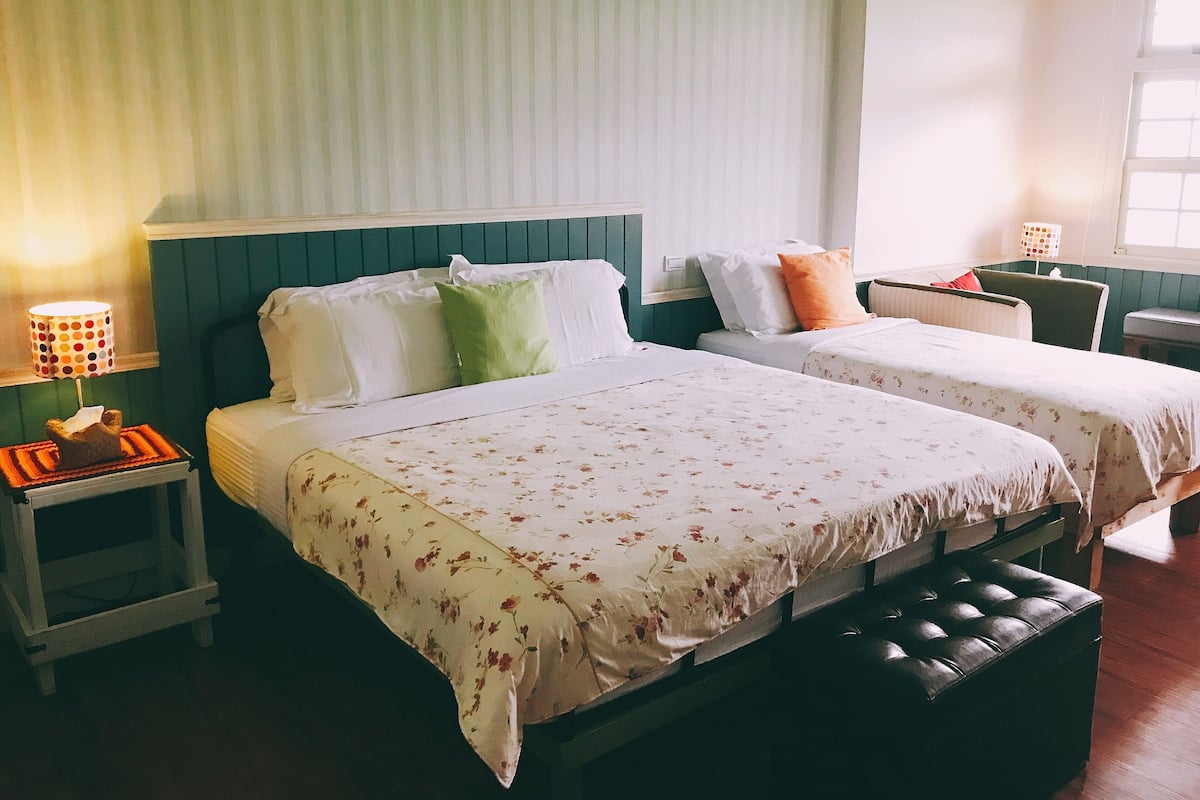 Quarto de hotel com duas camas, mesa de cabeceira, abajur e janela.