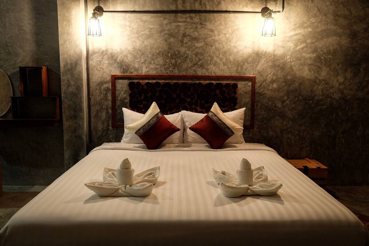 Cama bem arrumada com colcha listrada, dois travesseiros decorativos e duas toalhas dispostas em laço.