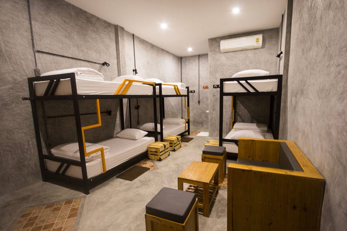 Quarto de dormitório com beliches, mesas de madeira e um pequeno banco de madeira.