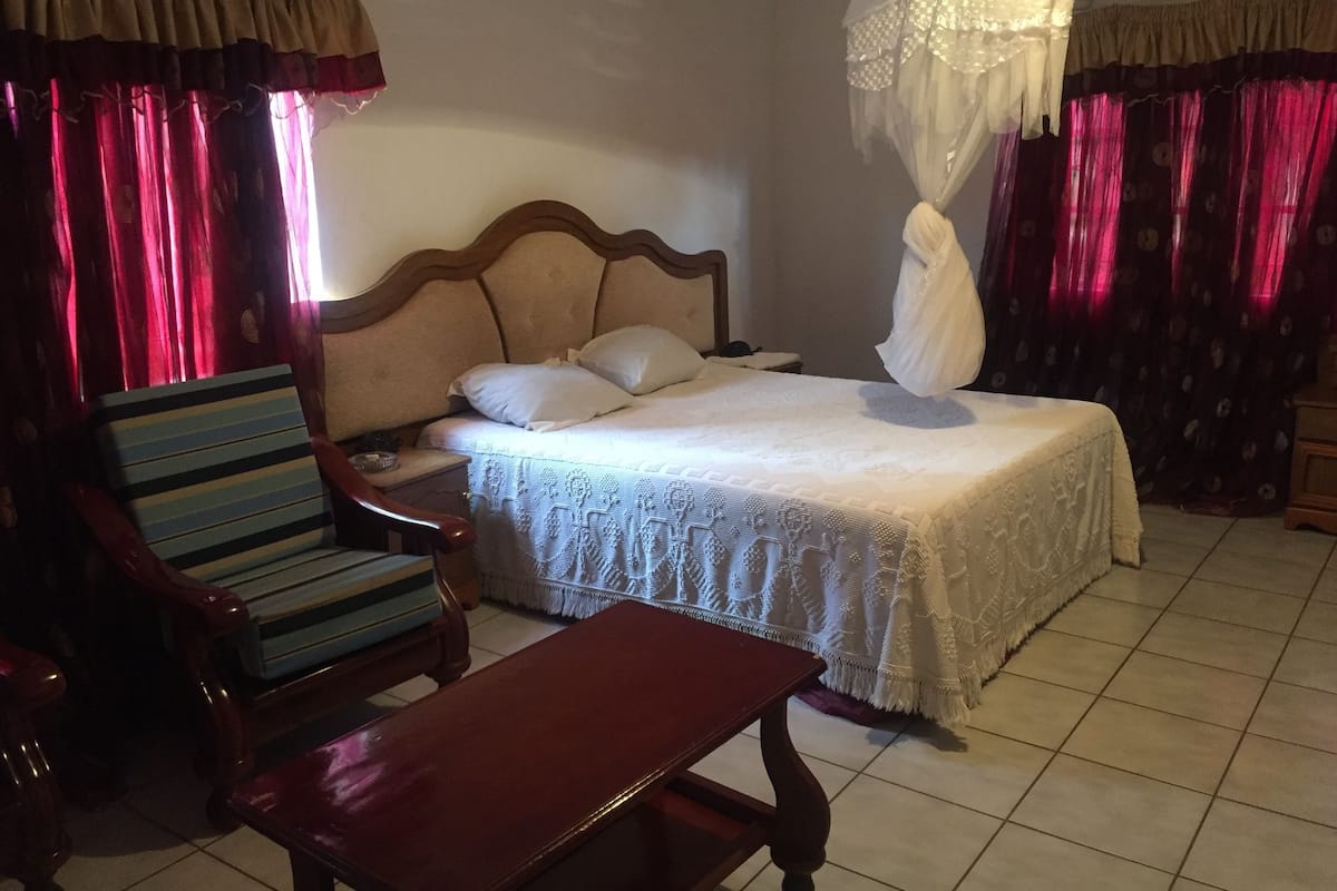 Um quarto com cama, uma cadeira, mesa de cabeceira e criado-mudo.