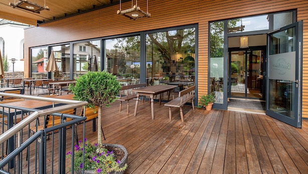 Um deck de madeira ao ar livre com mesas e bancos, janelas amplas e um lustre pendurado.