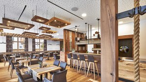 Um restaurante espaçoso com mesas e cadeiras de madeira, luminárias pendentes e um espaço de bar.