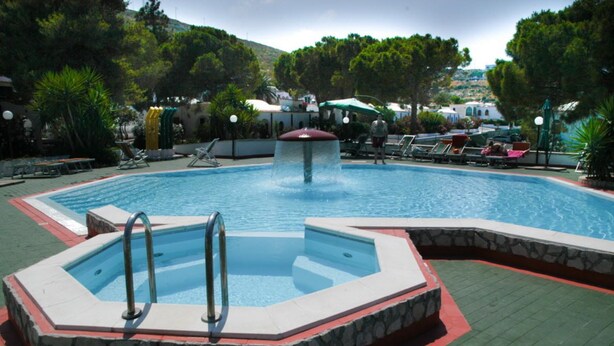 Piscina com hidromassagem, espreguiçadeiras e uma fonte.