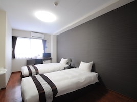Quarto de hotel com duas camas, uma escrivaninha, uma cadeira, um abajur e uma janela com cortinas.