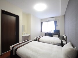 Quarto de hotel com duas camas, uma mesa de trabalho com televisão de tela plana, uma janela com cortinas e um aparelho de ar condicionado.