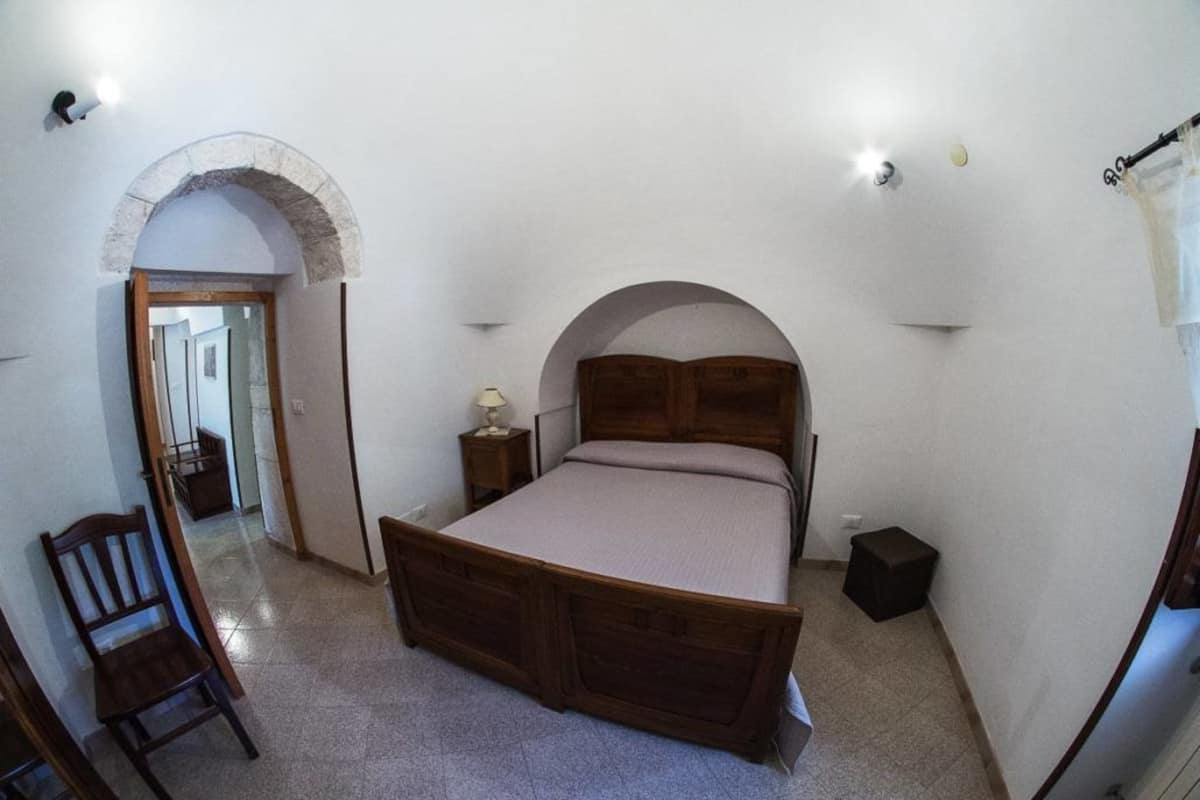 Quarto com cama de madeira, mesa de cabeceira, uma cadeira e uma pequena mesa.