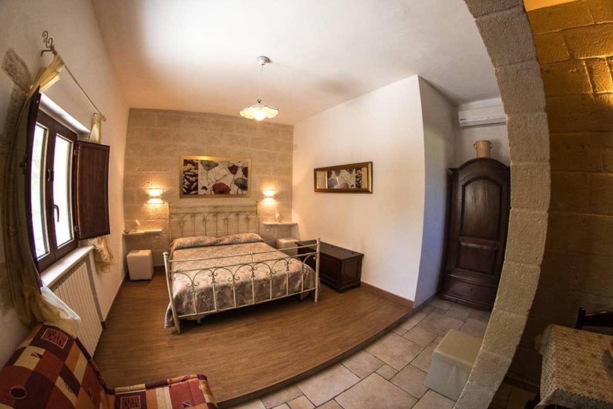 Um quarto com cama, mesas de cabeceira, janela, obra de arte na parede e um armário de madeira.