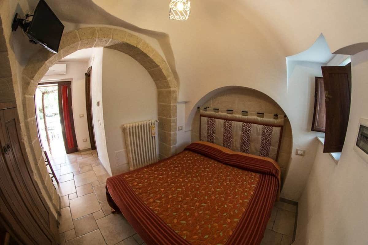 Quarto com cama, arcos de pedra, radiador e televisão fixada na parede.