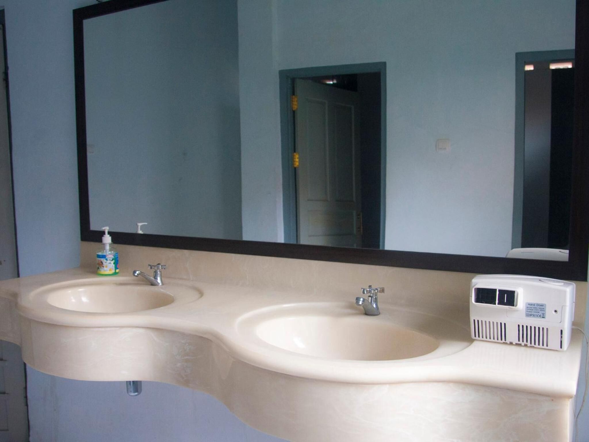 Casa de banho com duas pias, espelho e secador de mãos.