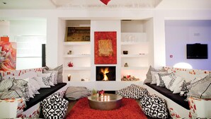 Uma sala de estar moderna com lareira, dois sofás com almofadas estampadas e um tapete vermelho.