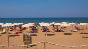 Uma praia com fileiras de guarda-sóis brancos e espreguiçadeiras, uma barreira de corda e o oceano ao fundo.