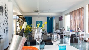 Uma área de jantar com uma mesa posta para dois, com uma garrafa de champanhe, taças de vinho e um vaso com flores amarelas.