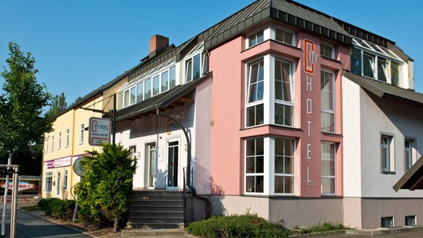 Um hotel de dois andares com fachada rosa, entrada visível e uma placa indicando ser um hotel urbano.