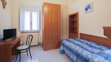 Um quarto com guarda-roupa de madeira, uma cama com colcha azul estampada, uma escrivaninha com televisão e uma cadeira.