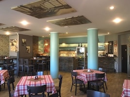 Um restaurante com mesas cobertas por toalhas xadrez vermelhas e brancas, cadeiras de madeira e um bar com balcão de pedra.