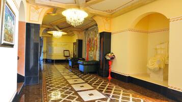 Um hall de hotel com piso estampado, balcão de recepção, uma estátua e um lustre.
