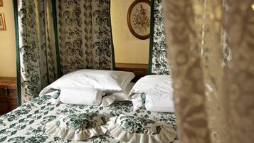 Uma cama com lençóis brancos e estampas florais verdes, uma cabeceira de madeira e uma obra de arte floral emoldurada na parede.