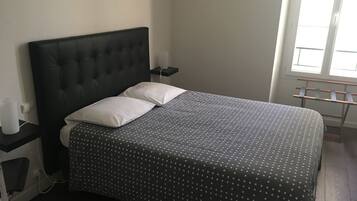 Quarto com cabeceira escura, cama com colcha de bolinhas, almofadas brancas, mesa de cabeceira com abajur e um quadro na parede.