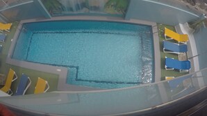 Piscina com mural de cachoeira, cadeiras de descanso e vista para motocicletas estacionadas.