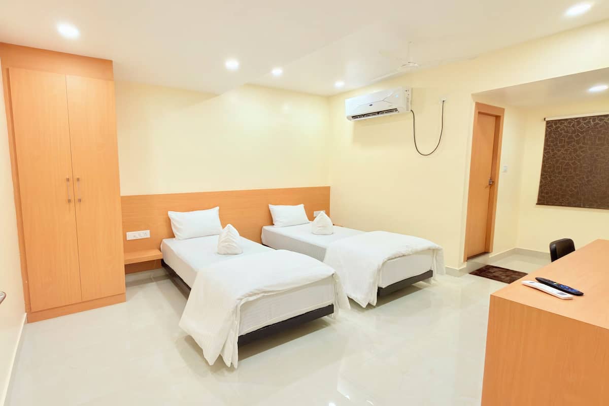 Quarto de hotel com duas camas de solteiro, um guarda-roupa de madeira, uma escrivaninha com cadeira e um aparelho de ar condicionado.
