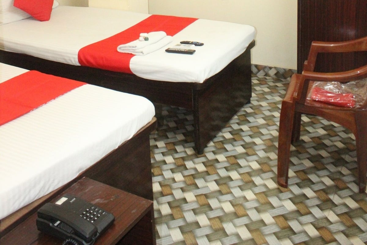 Quarto de hotel com duas camas de solteiro, um guarda-roupa de madeira, uma cadeira de madeira e um projetor sobre uma pequena mesa.