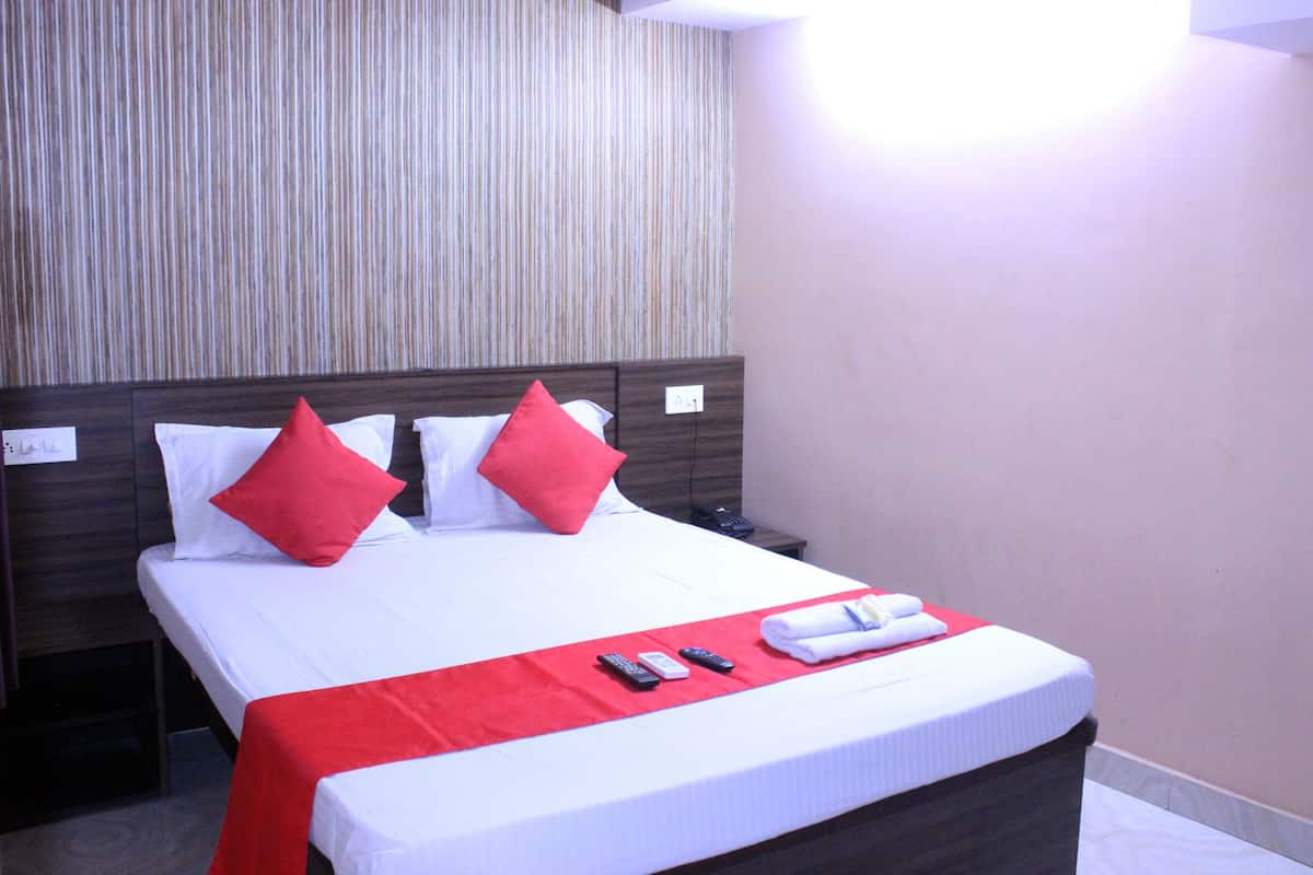 Quarto de hotel com cama, mesa de cabeceira e luminária fixada na parede.