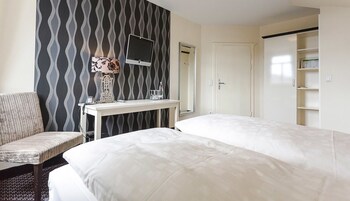 Quarto de hotel com duas camas, uma escrivaninha com abajur, uma cadeira, televisão, guarda-roupa e estante de livros.
