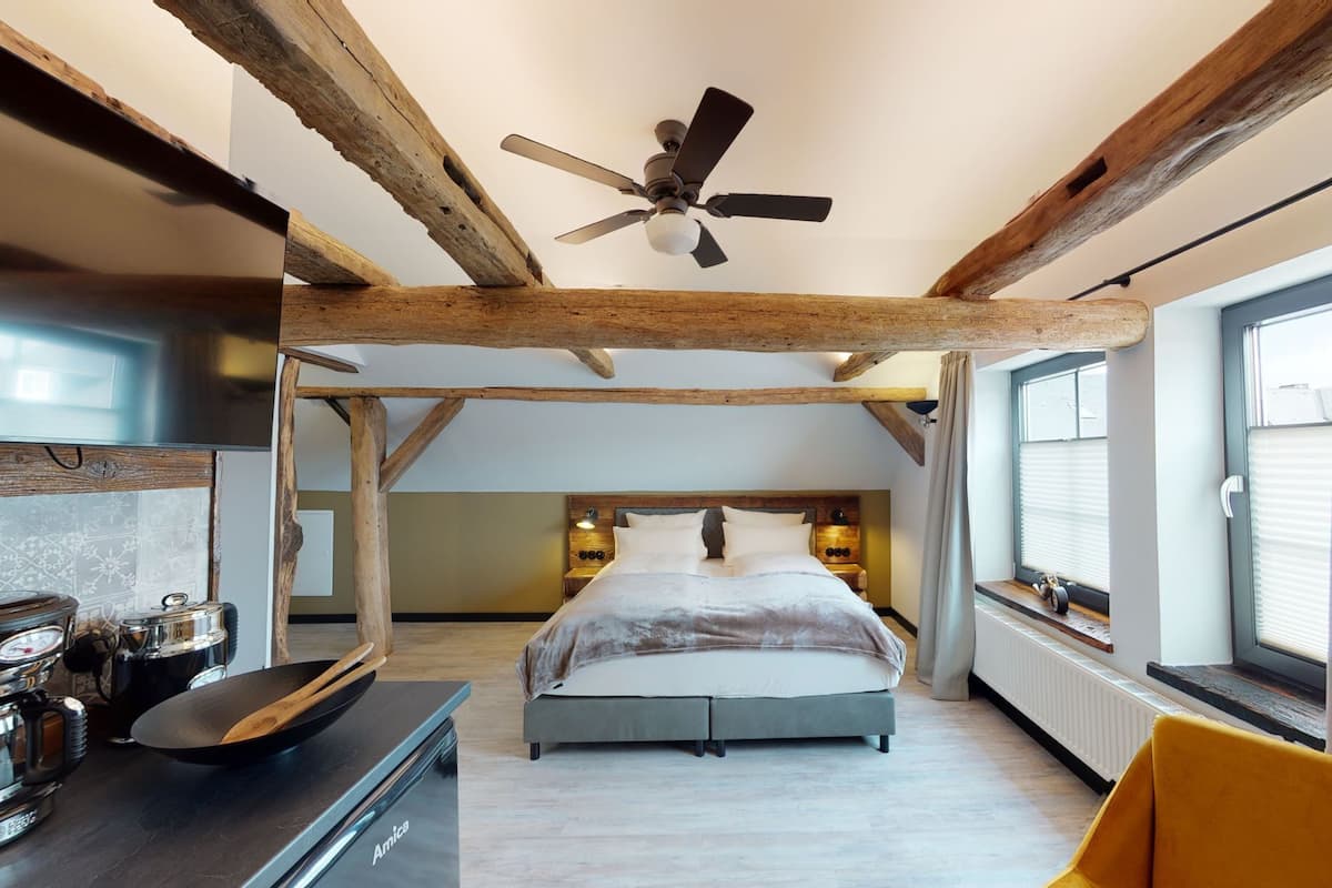 Quarto com cama, ventilador de teto, janela com cortinas e cozinha equipada com fogão e utensílios.